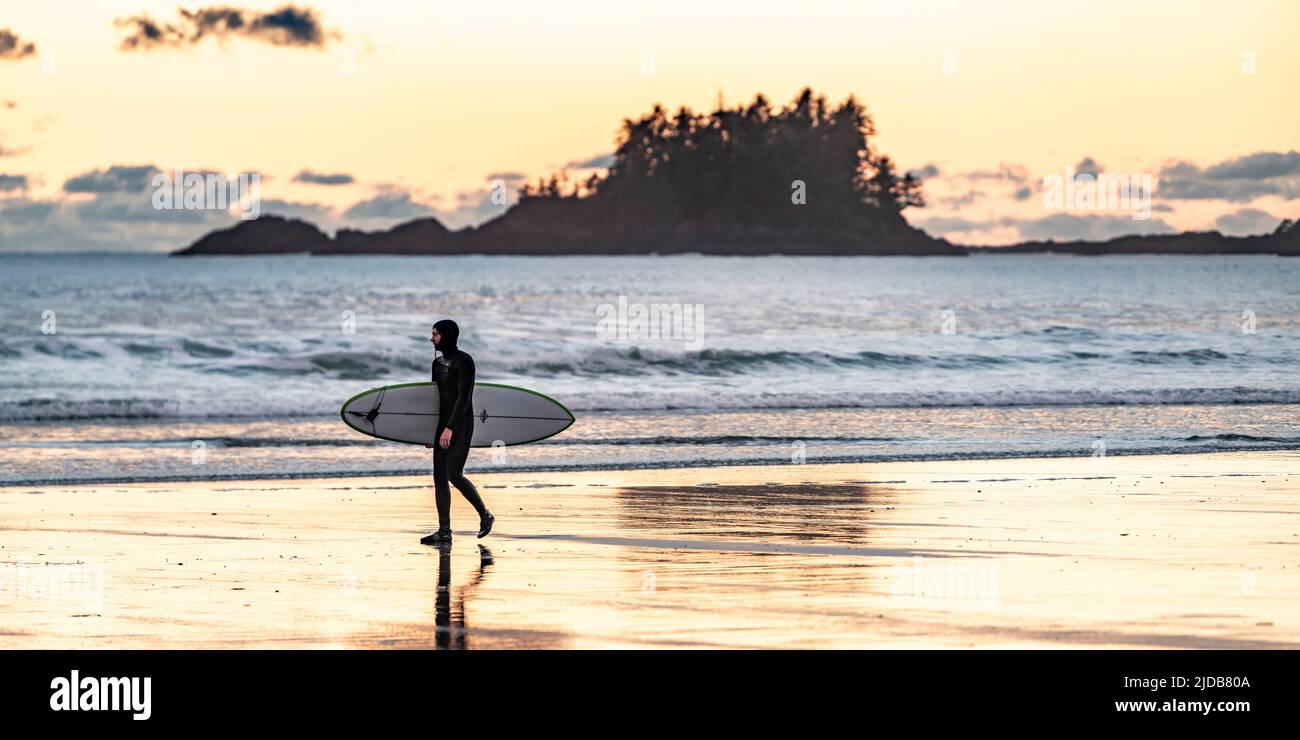 A surfer carries their surfboard on the wet sand at the popular surfing ...
