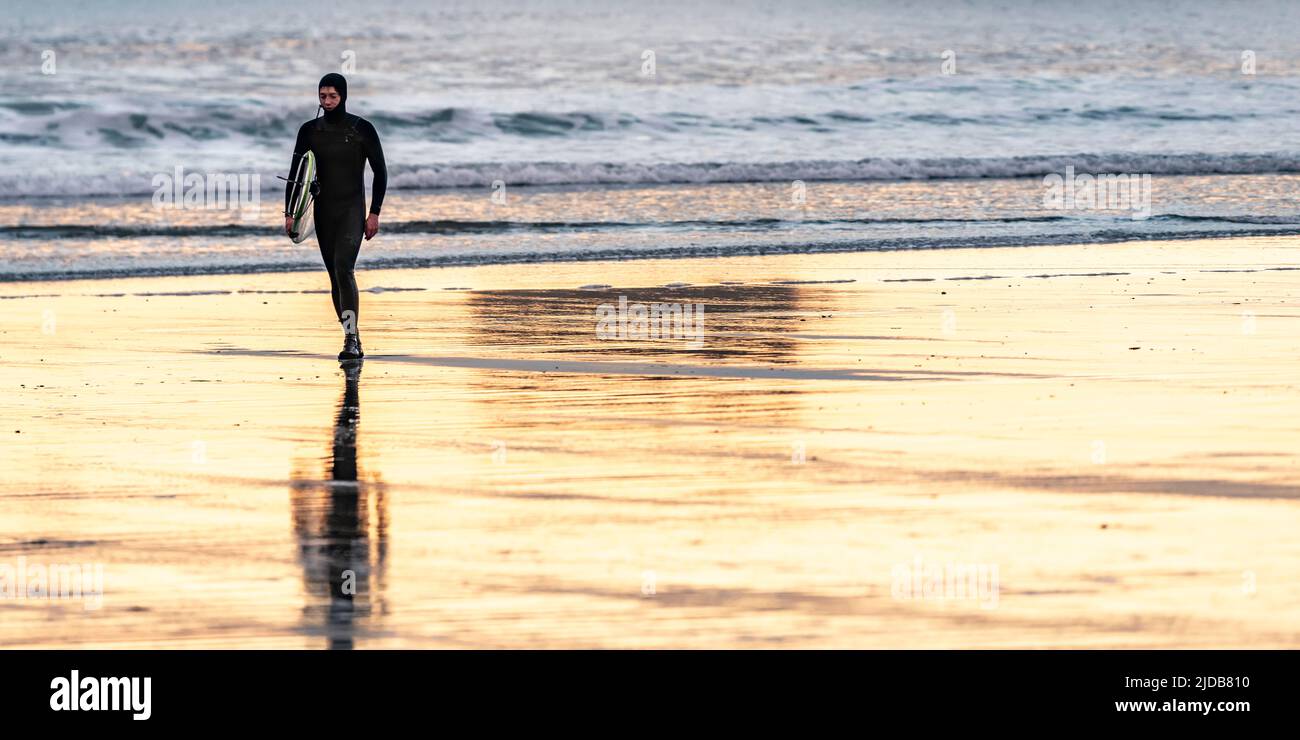 A surfer carries their surfboard on the wet sand at the popular surfing ...