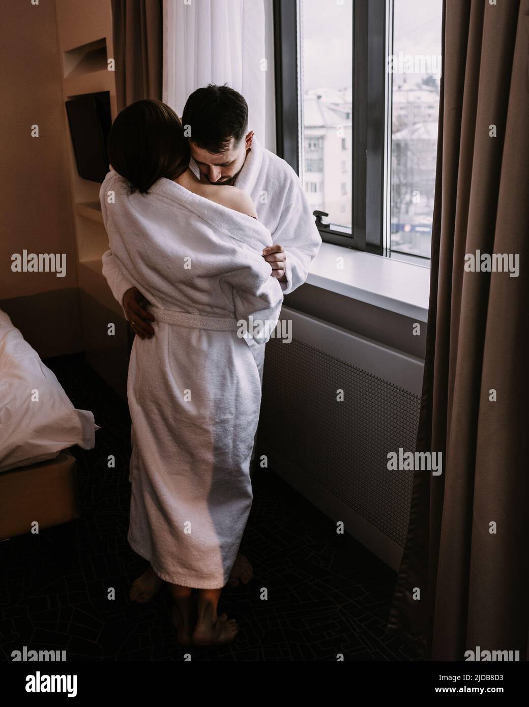 Happy couple in the hotel on window hug each other Man gently kissing ...