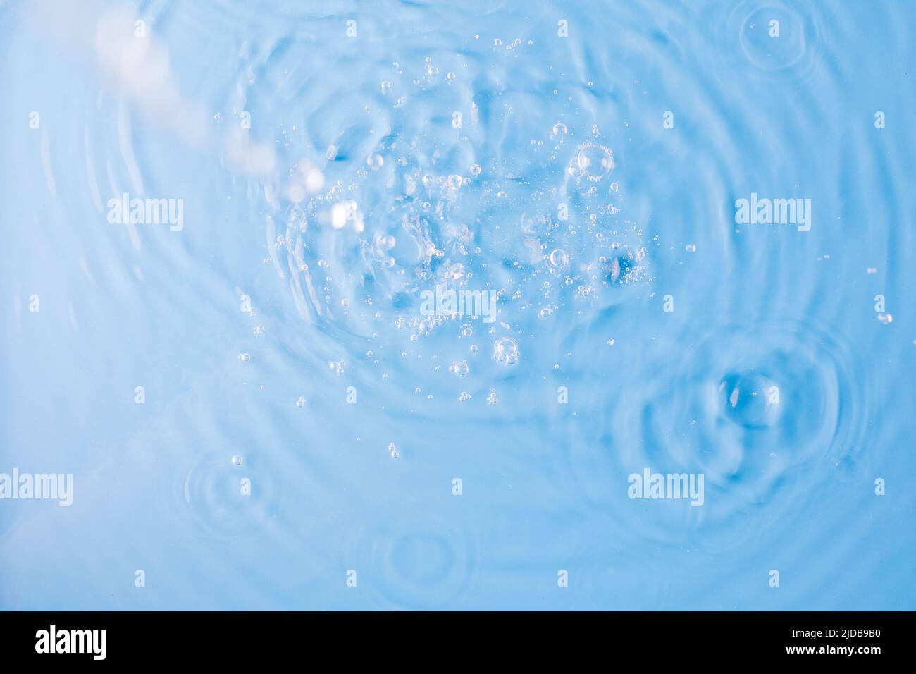 Pouring and splashing clear water on light blue background upper close ...