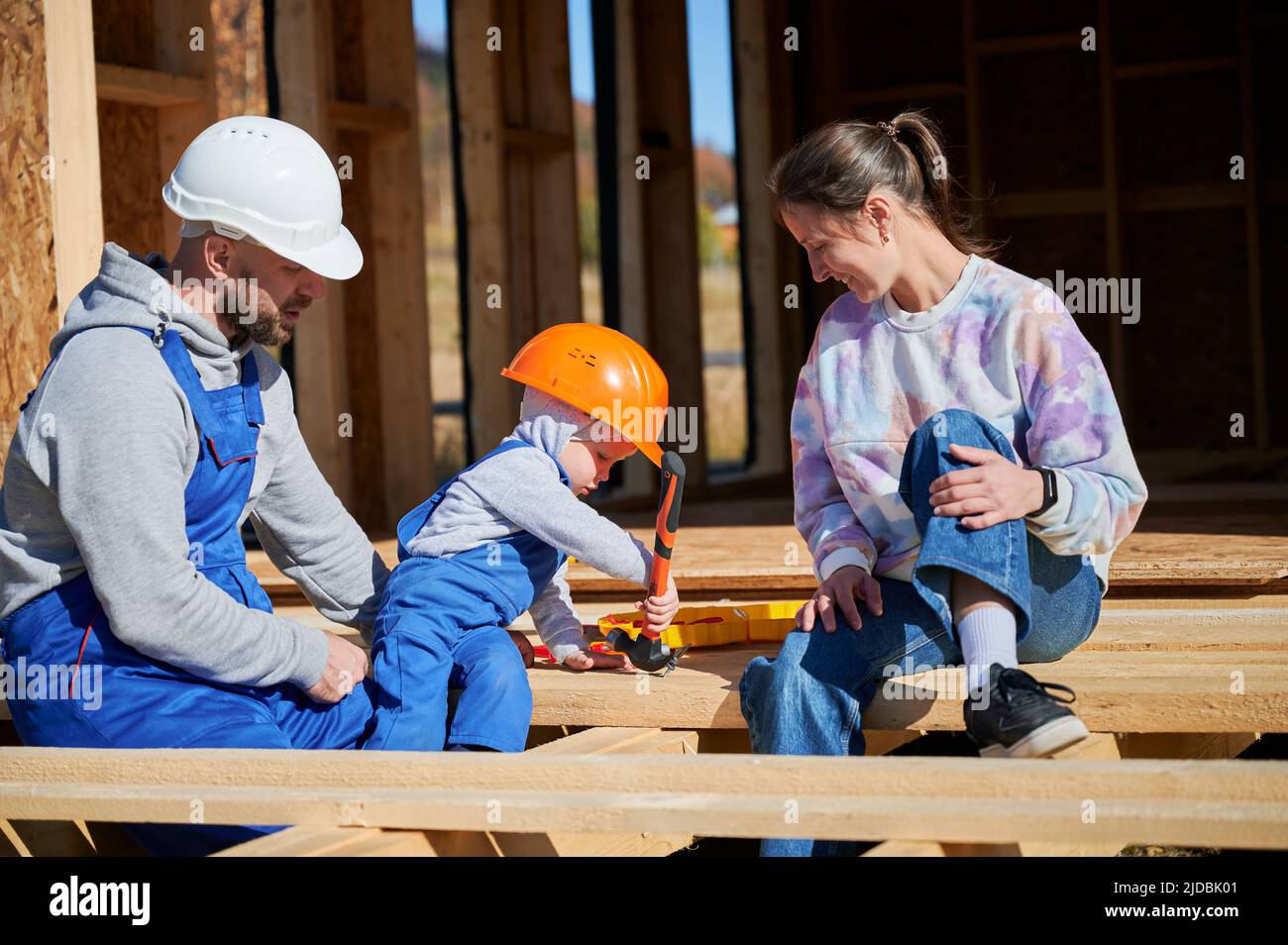 Father, mother and son building wooden frame house. Toddler boy helping ...