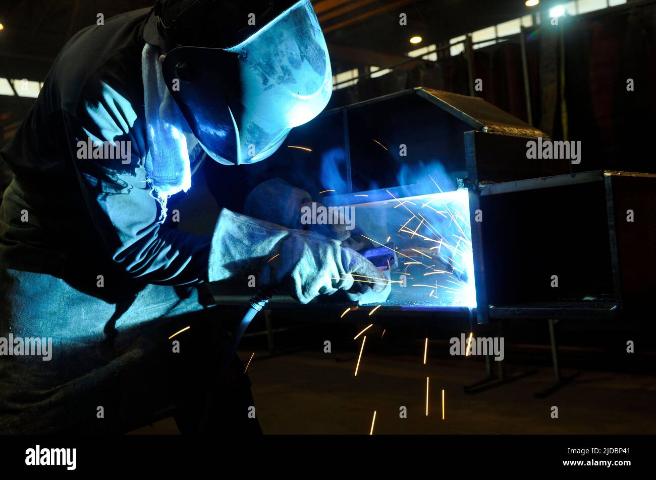 A welder in protective overalls and a welding mask welds metal ...