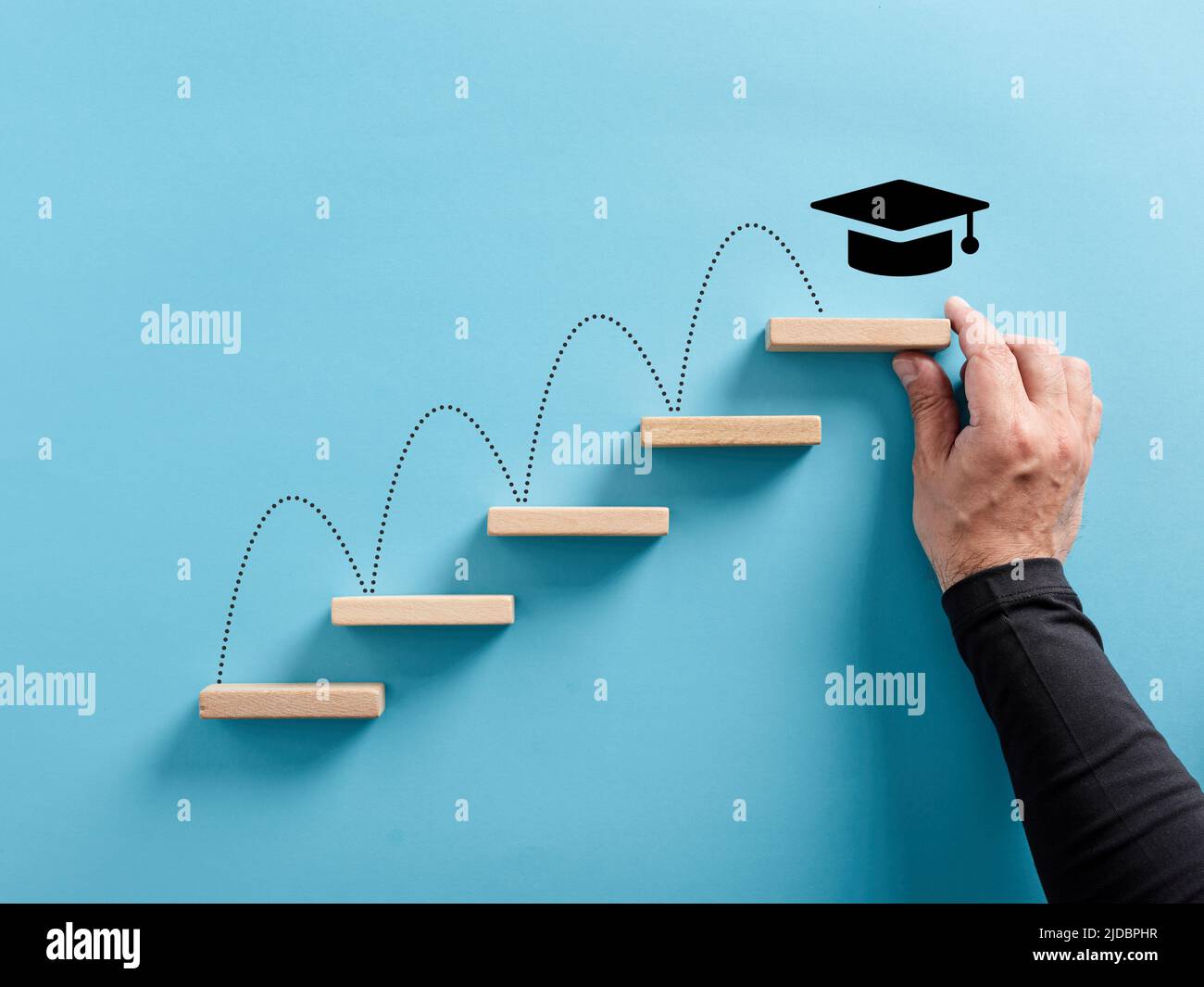 Male hand arranges a wooden block ladder with academic cap symbol ...