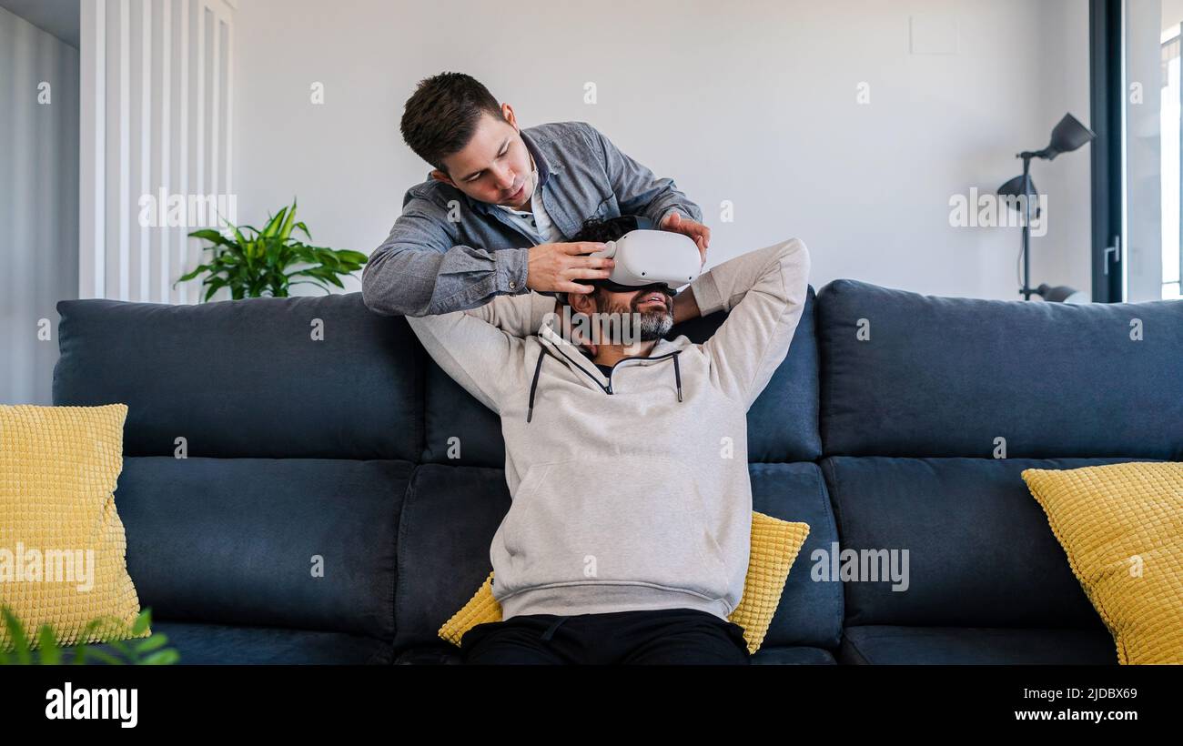 Caucasian men enjoying virtual reality glasses while sitting on sofa at ...