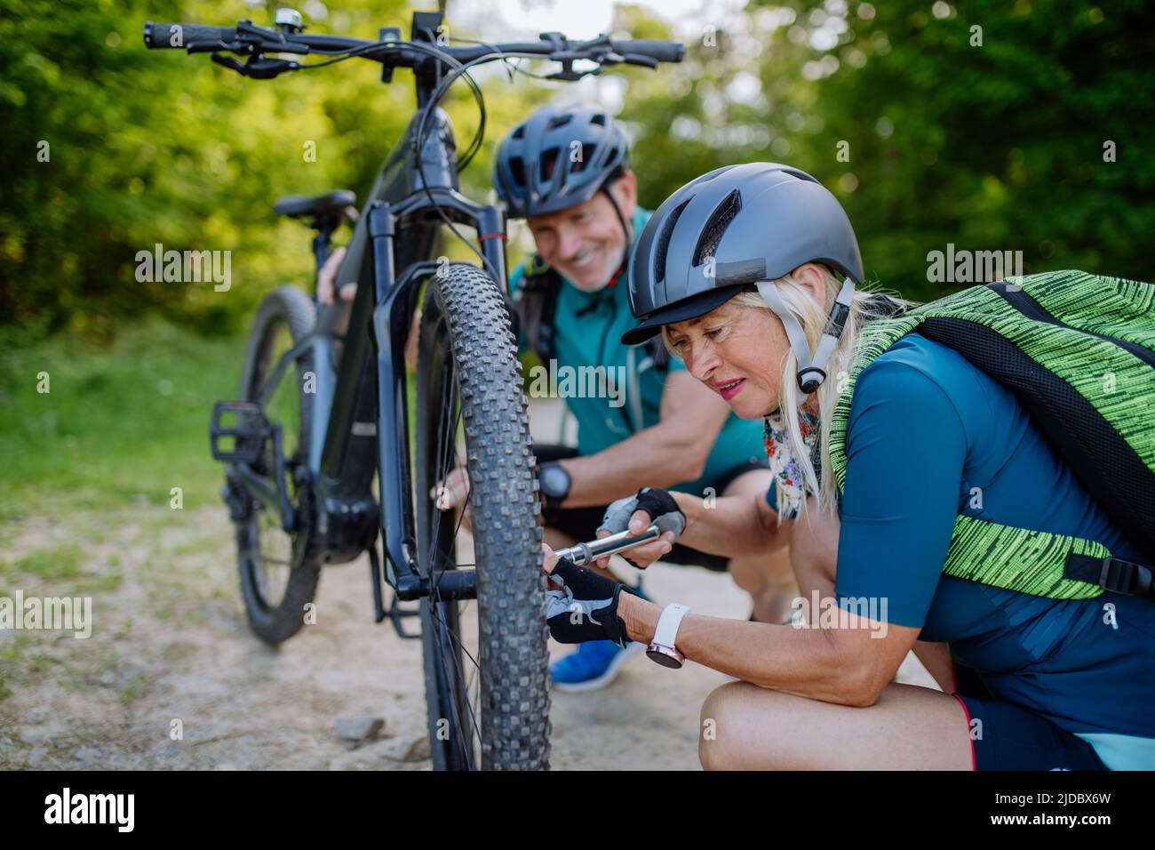 Active senior couple repairing bicycle, pumping up tire in nature in ...