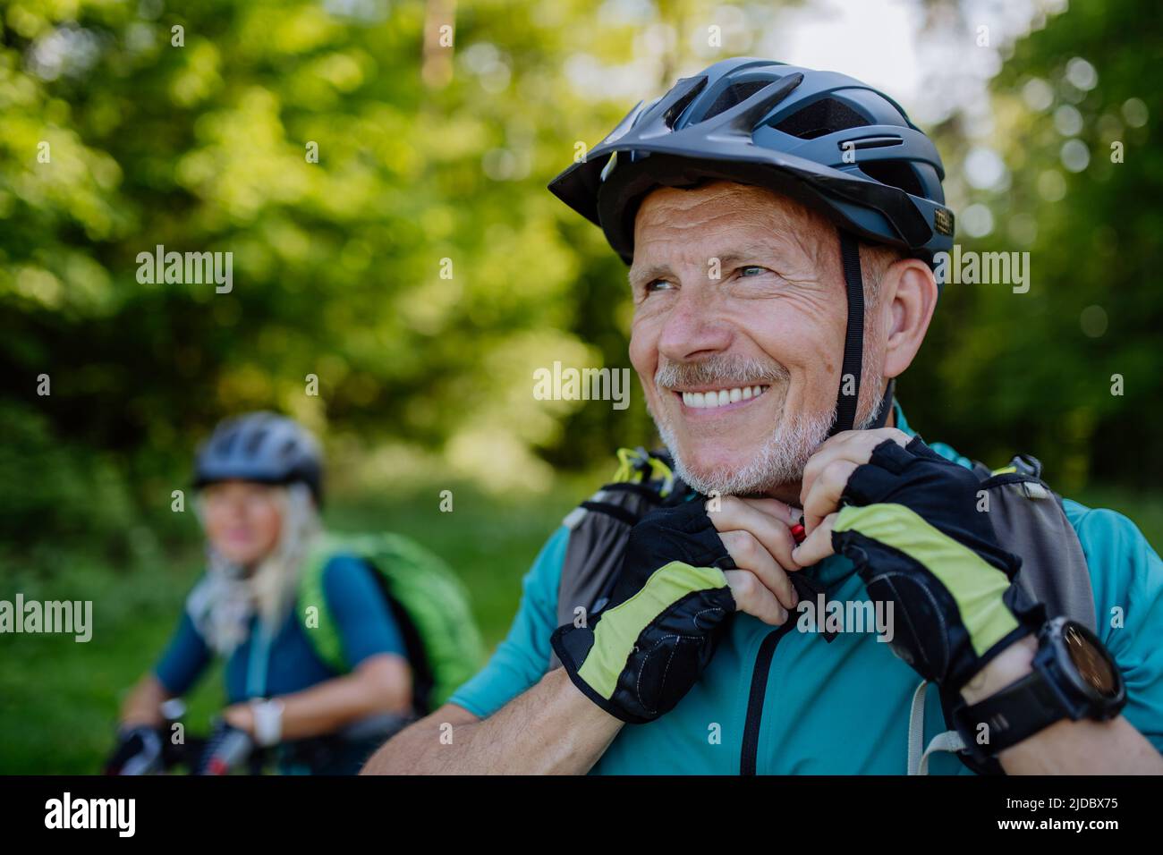 Active senior couple riding bicycles at summer park, man is putting on ...