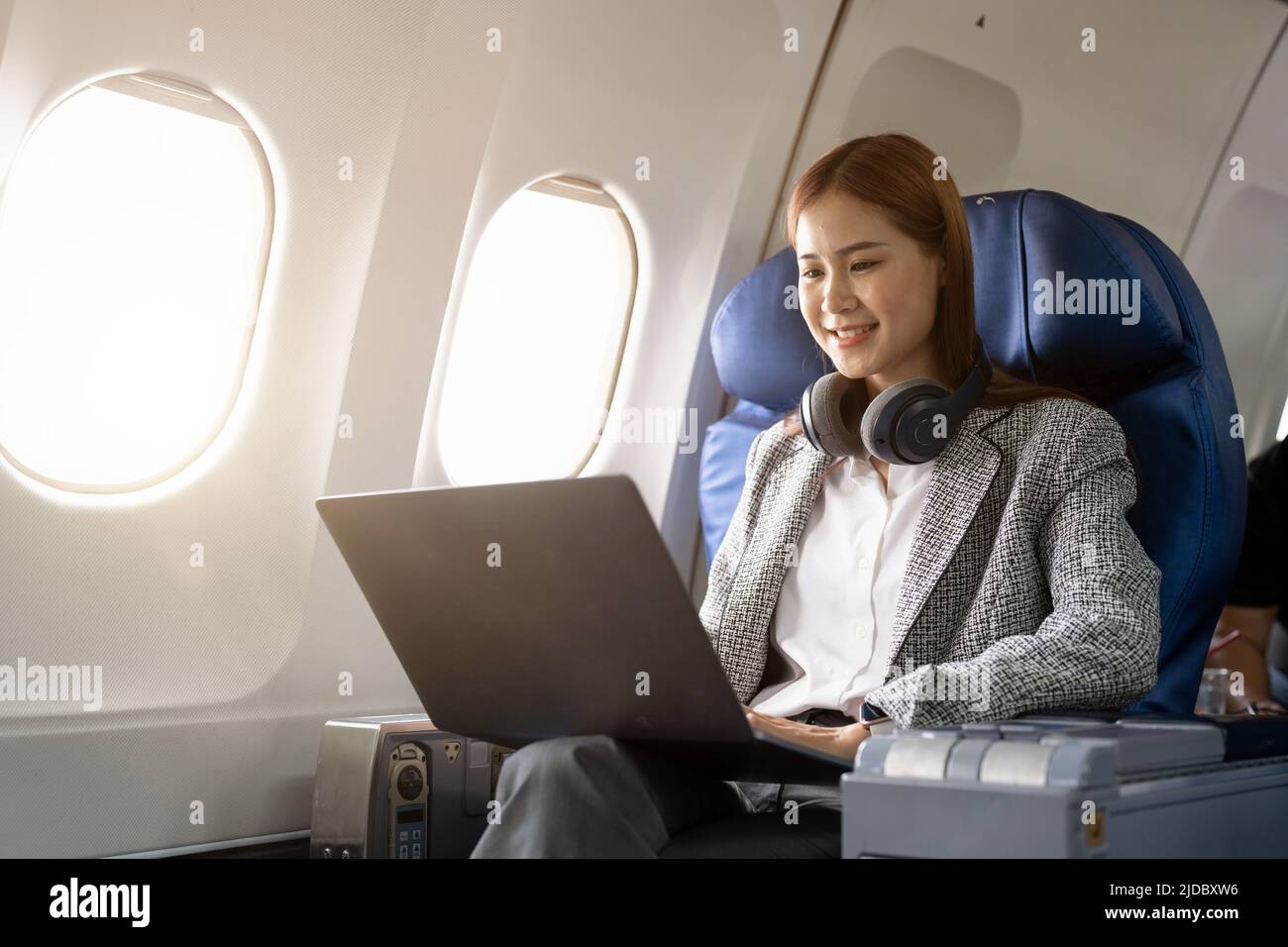 Asian young woman wearing headphone using laptop sitting near windows ...