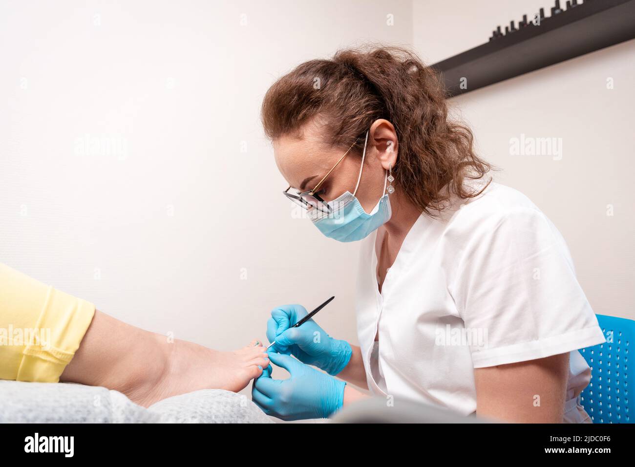 Woman podiatrist in blue gloves does a caring procedure for the client ...