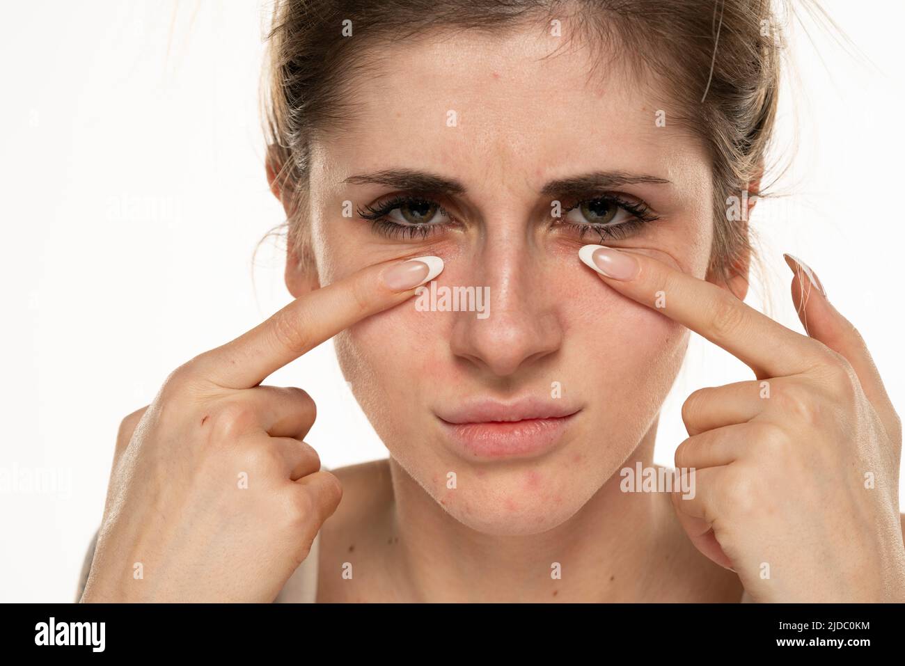 Beautiful young woman touch her face under eyes on white background ...