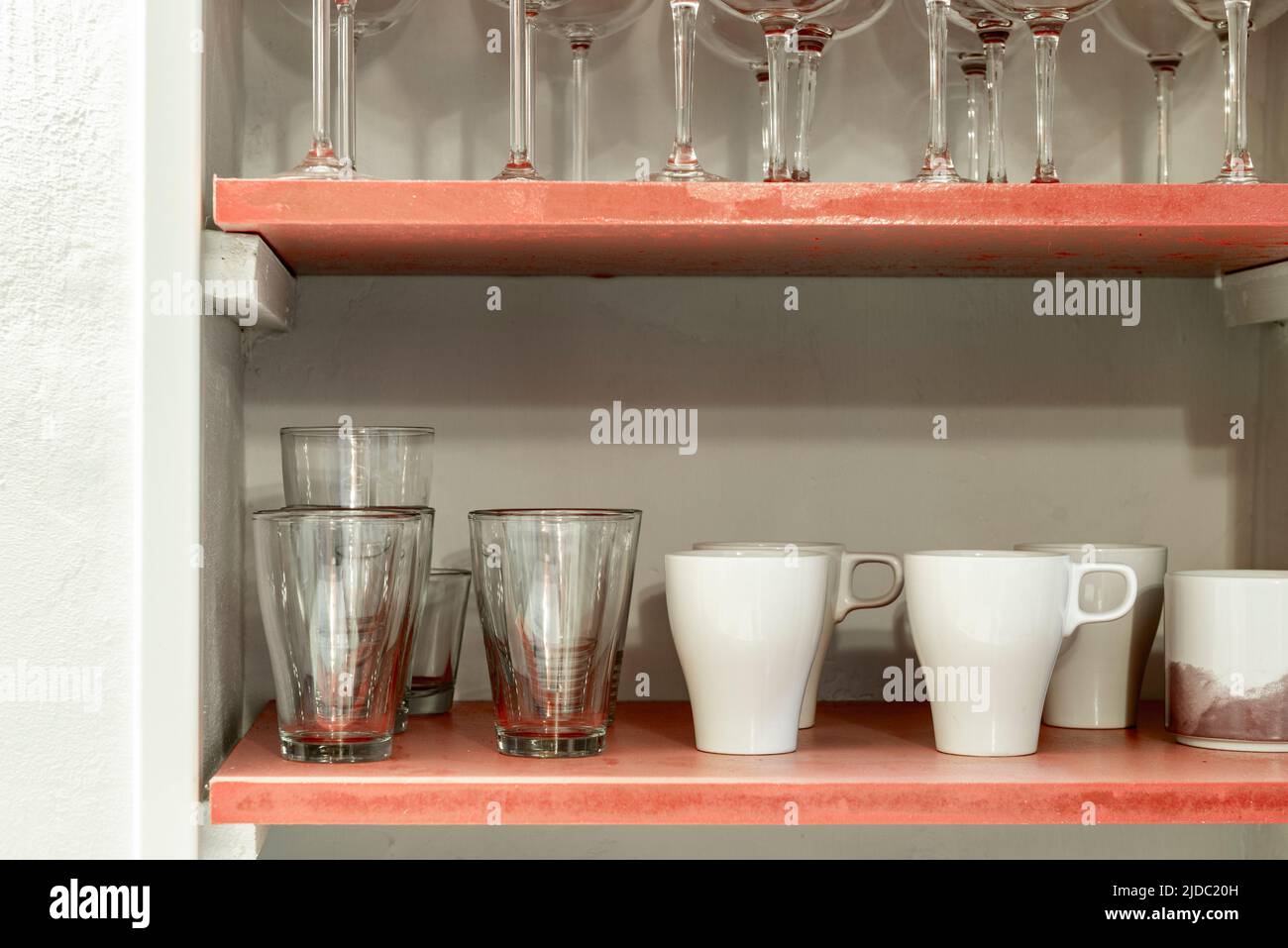 Cupboard with light red shelves filled with china and crystal mugs ...