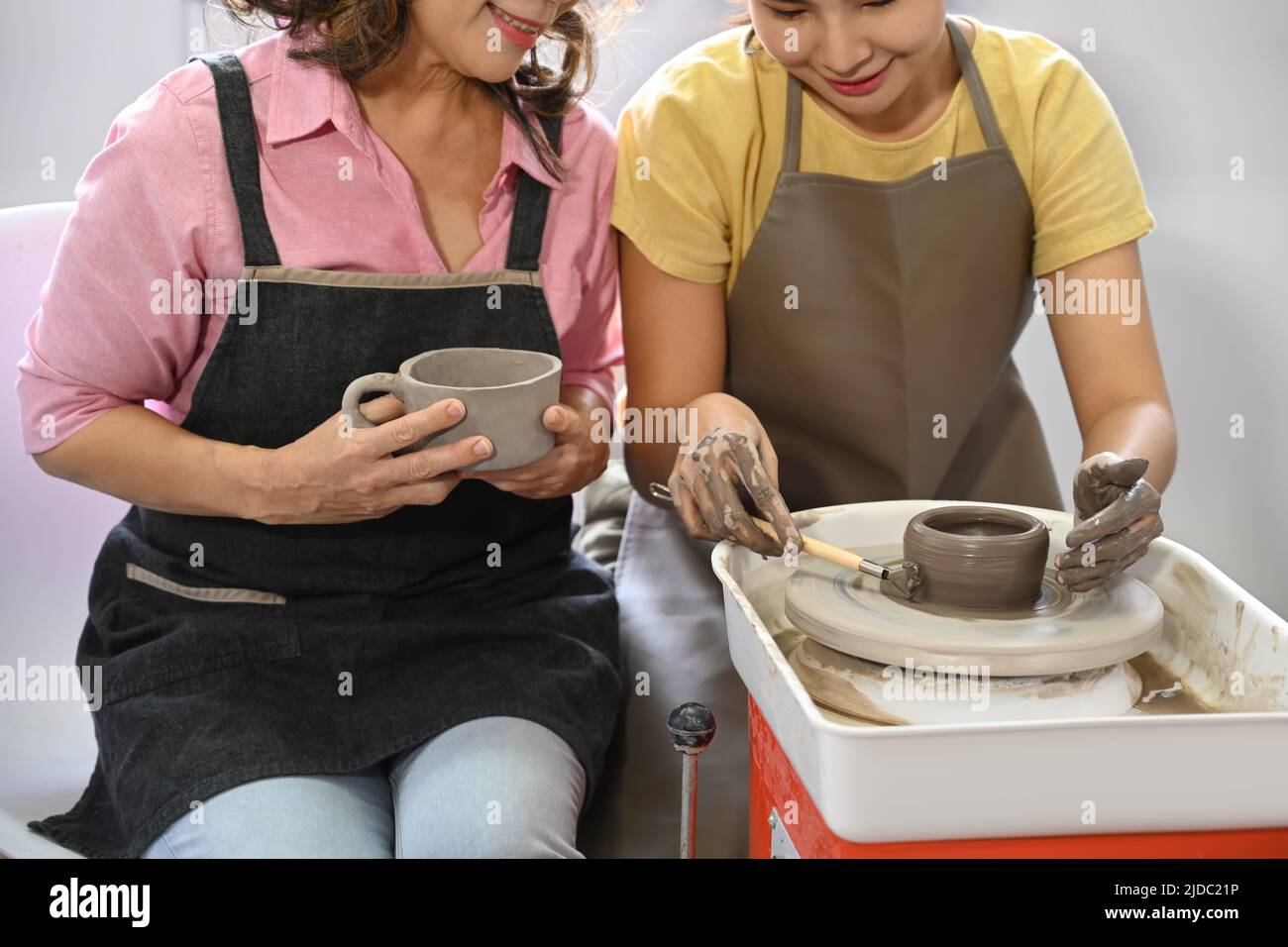 Young woman teaching middle aged woman making ceramics in pottery ...