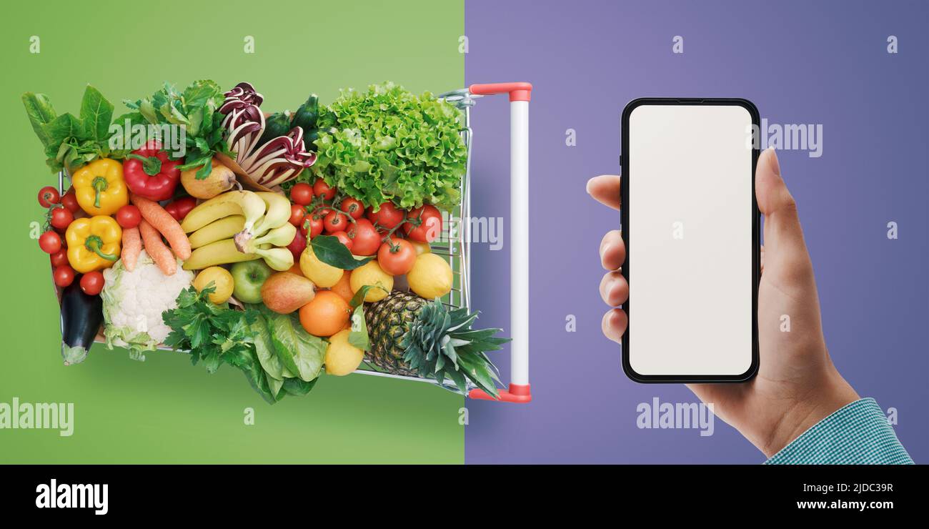 Customer holding a smartphone with blank screen and shopping cart full ...