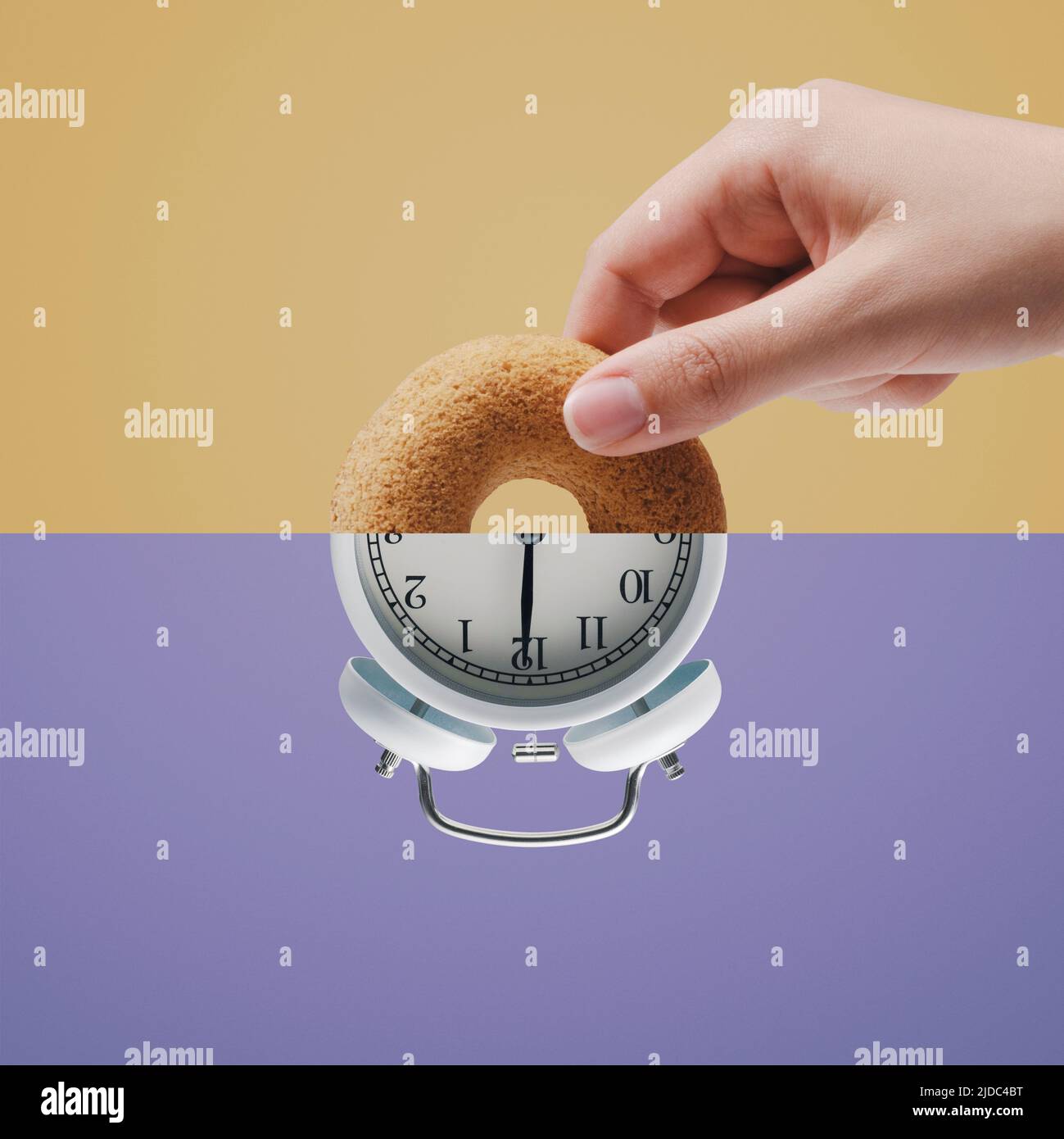 Half alarm clock and hand holding a donut shaped cookie, it's snack ...