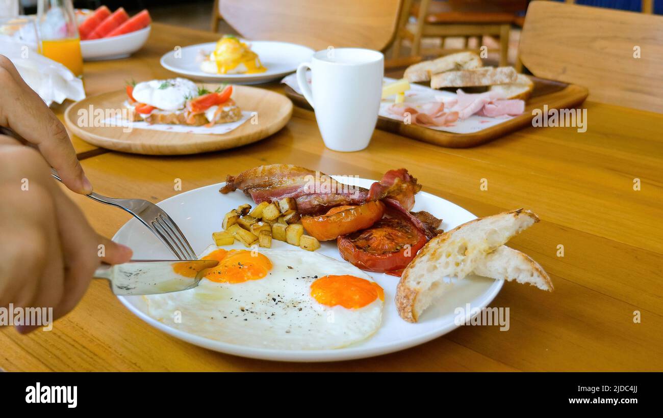 Man eat fried egg with toasted bread, bacon and tomatoes in cafe ...