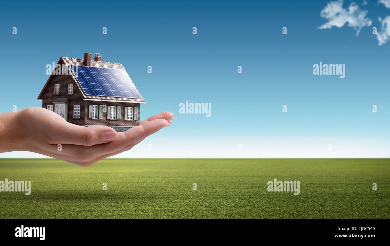 Hand holding an energy efficient model house with solar panels, ecology ...