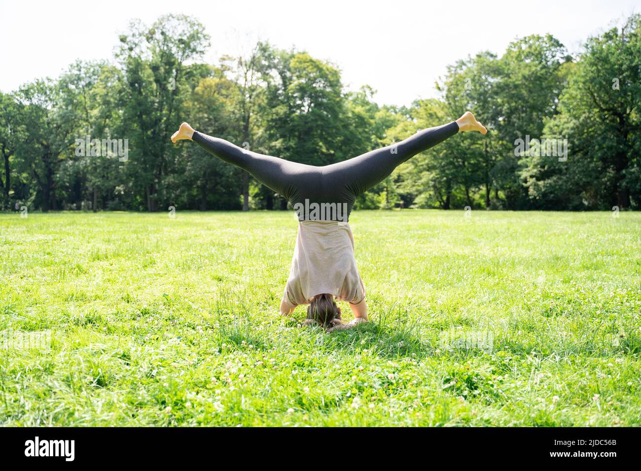 Young woman standing on her head doing headstand split yoga pose in ...