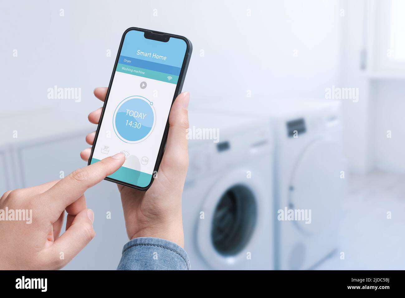 Woman controlling her smart washing machine from her smartphone, she is ...