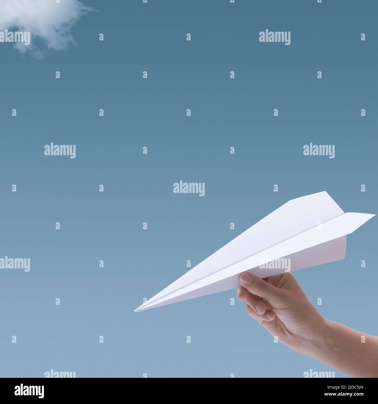 Woman holding a paper airplane and blue sky in the background ...