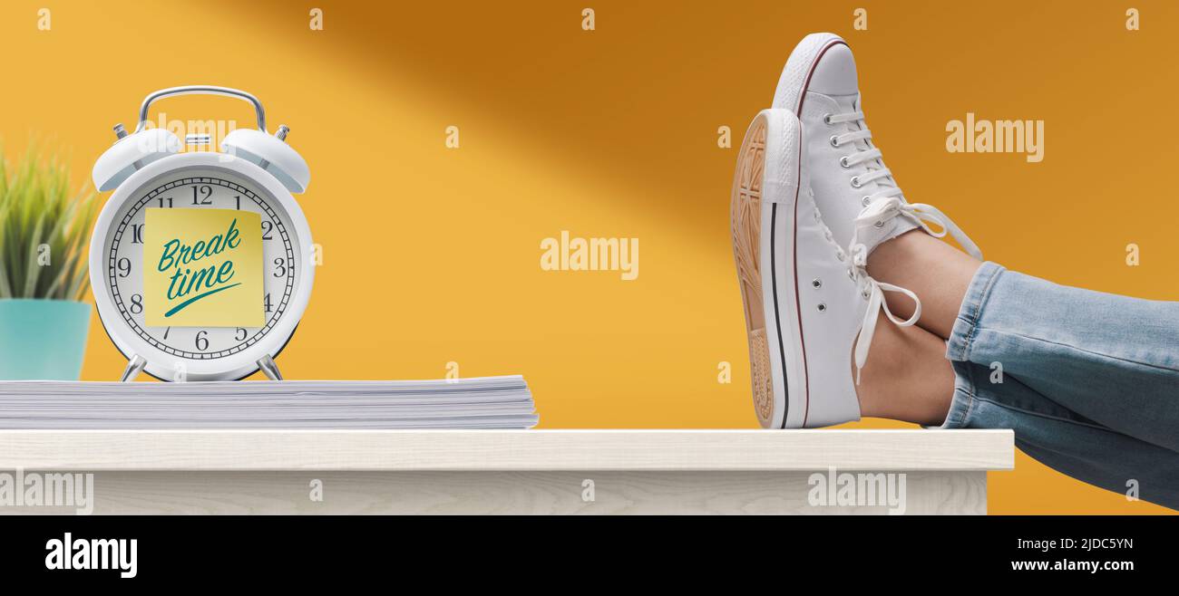 Woman with feet up on a desk and alarm clock with sticky note, it's ...