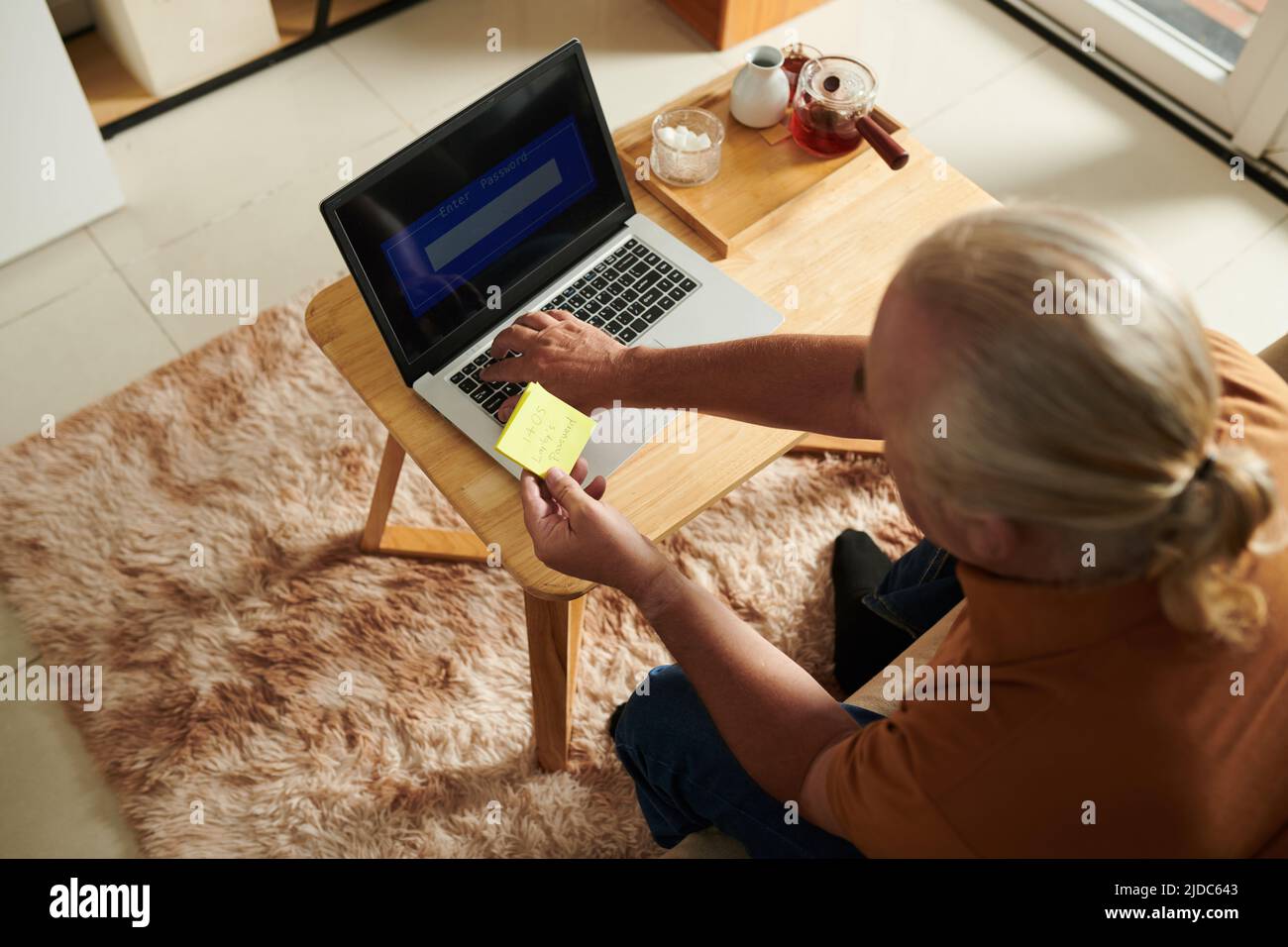 Senior man entering password written on sticky note when logging in ...