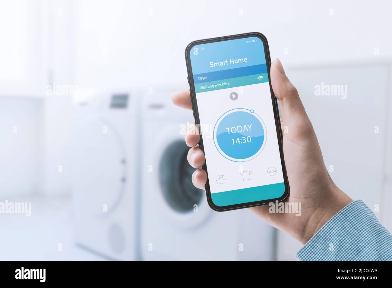 Woman controlling her smart washing machine from her smartphone, she is ...
