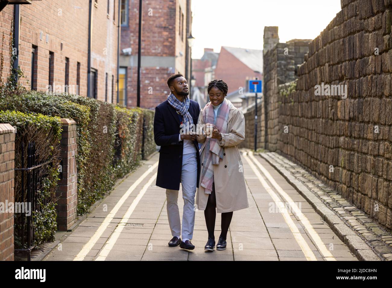 Couple walking along back lane alongside old stone wall, woman holding ...