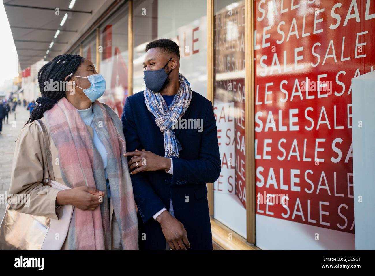 Couple wearing face coverings shopping, passing shop window with Sale ...