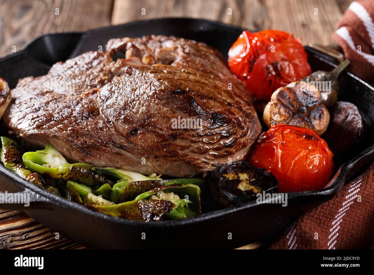 Large piece of grilled meat with vegetables in a cast iron pan, close ...