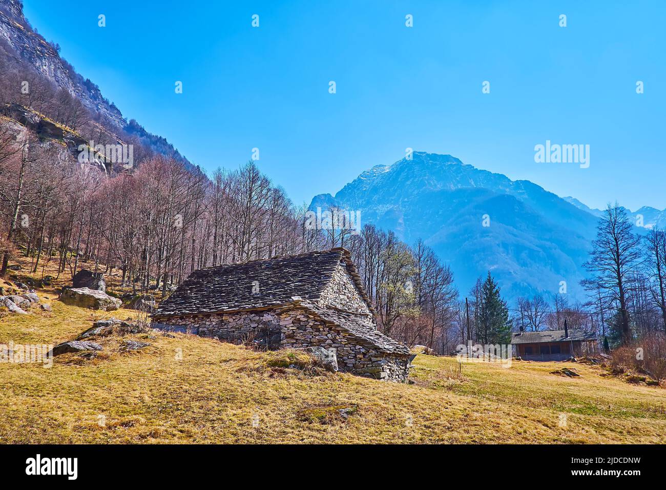 The small mountain meadow with dry yellow grass, small stone barn and ...