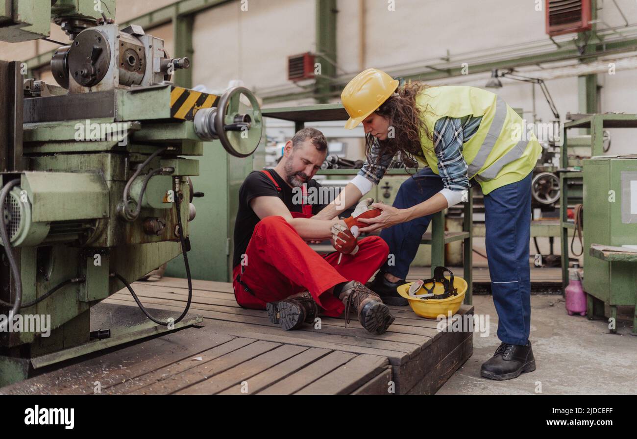 Woman is helping her colleague after accident in factory. First aid ...