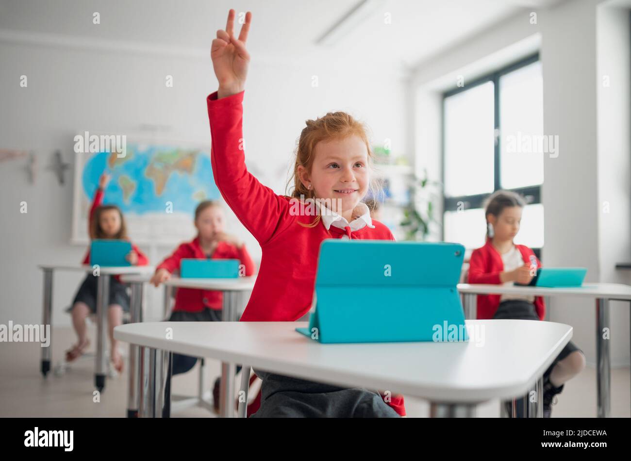Happy schoolgirl with hands up using digital tablet during lesson in ...