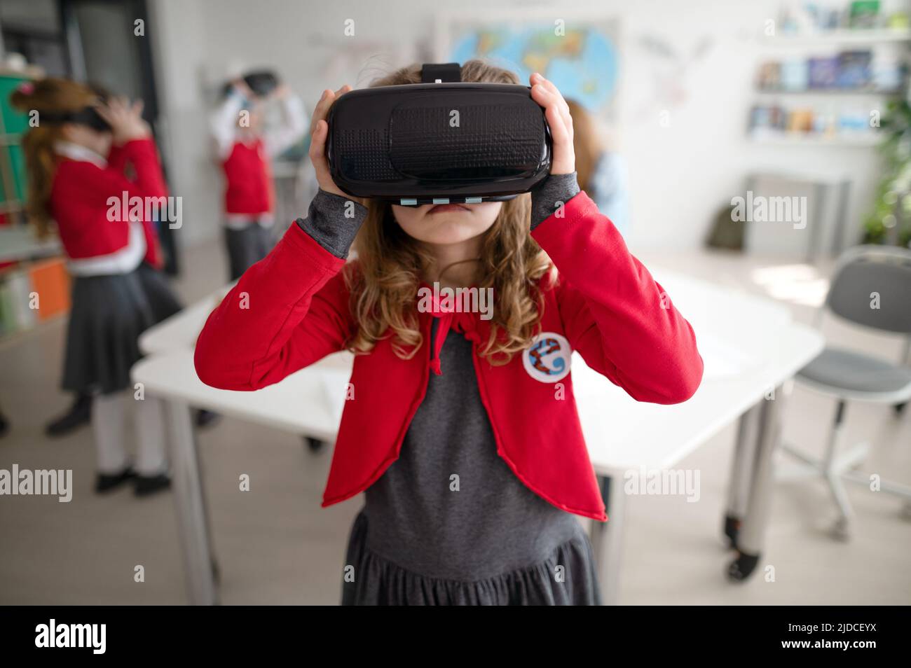 Happy schoolgirl wearing virtual reality goggles at school in computer ...