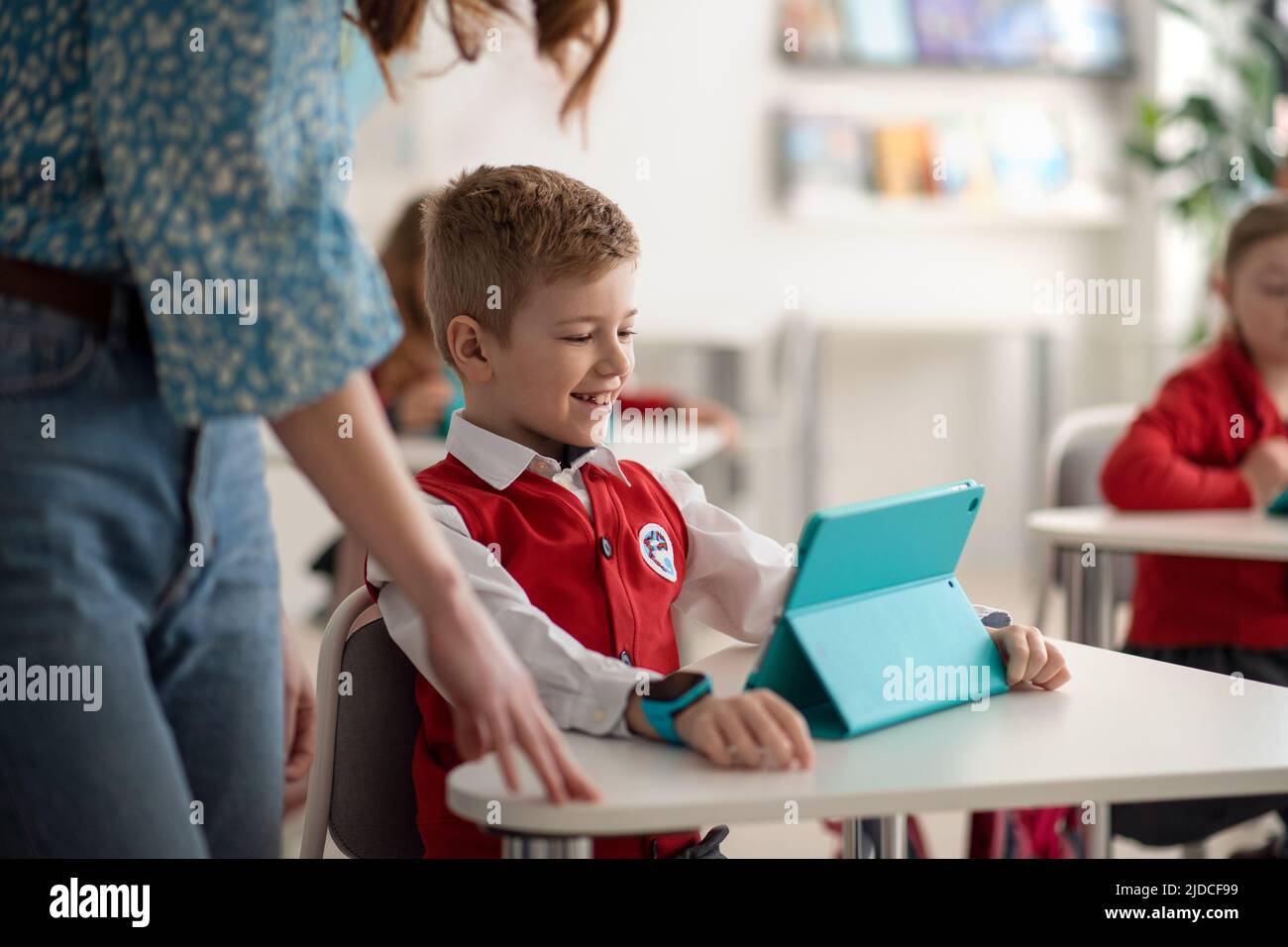 Happy schoolboy using digital tablet during lesson in classroom at ...