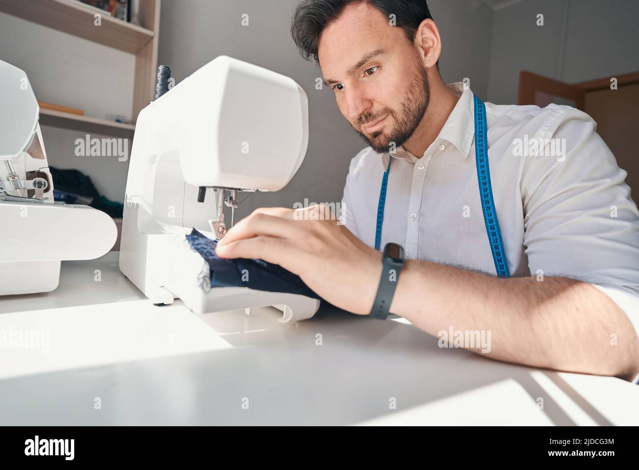 Smiling man fashion designer sewing with equipment Stock Photo - Alamy