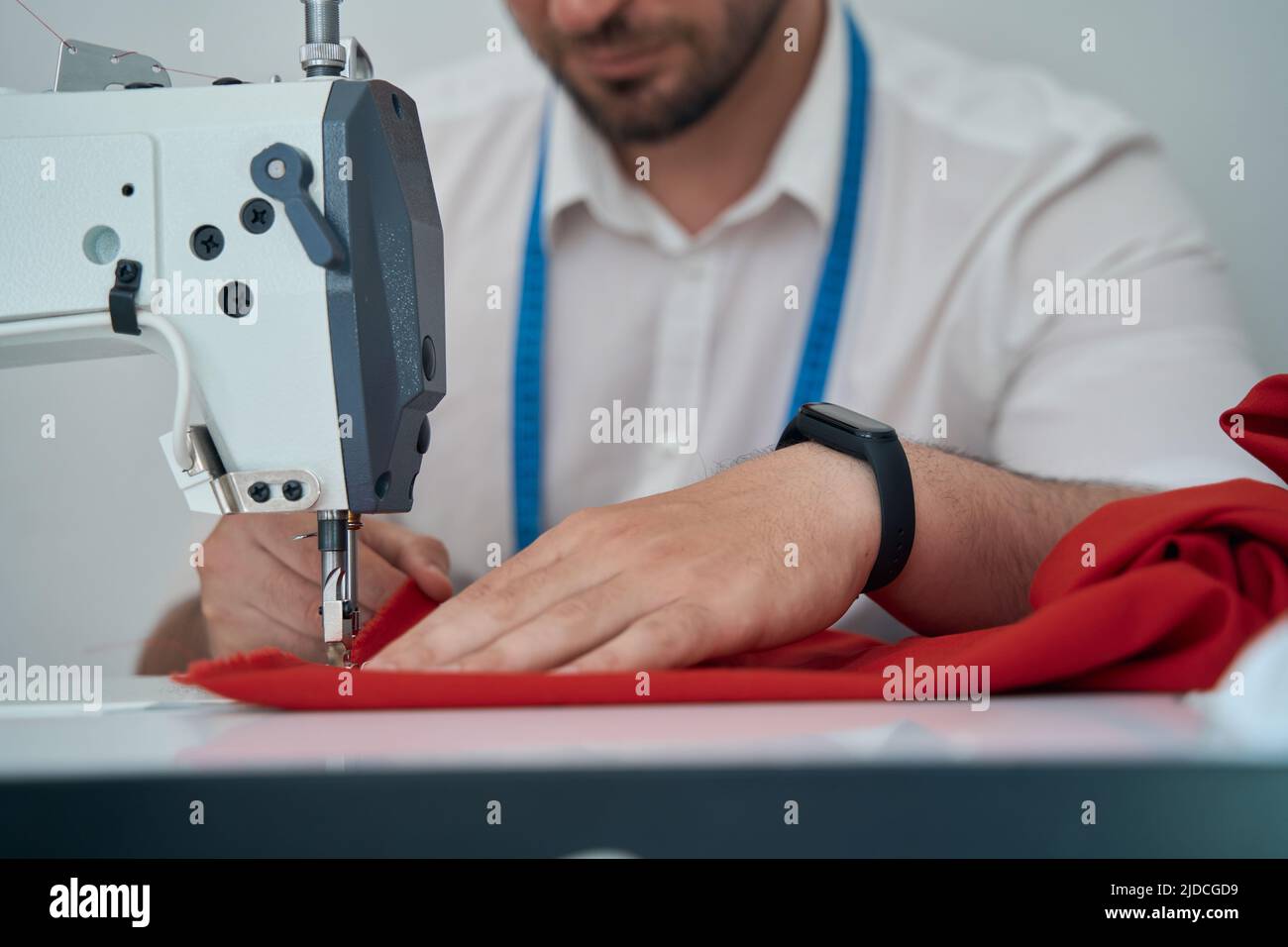 Smiling tailor with smartwatch using sewing machine Stock Photo - Alamy