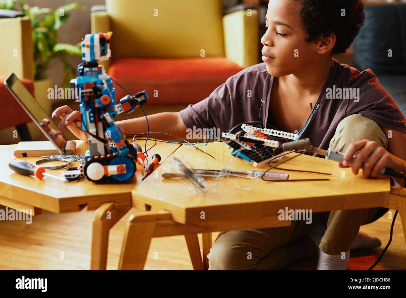 A smart African-American boy holding soldering iron and touching tablet ...