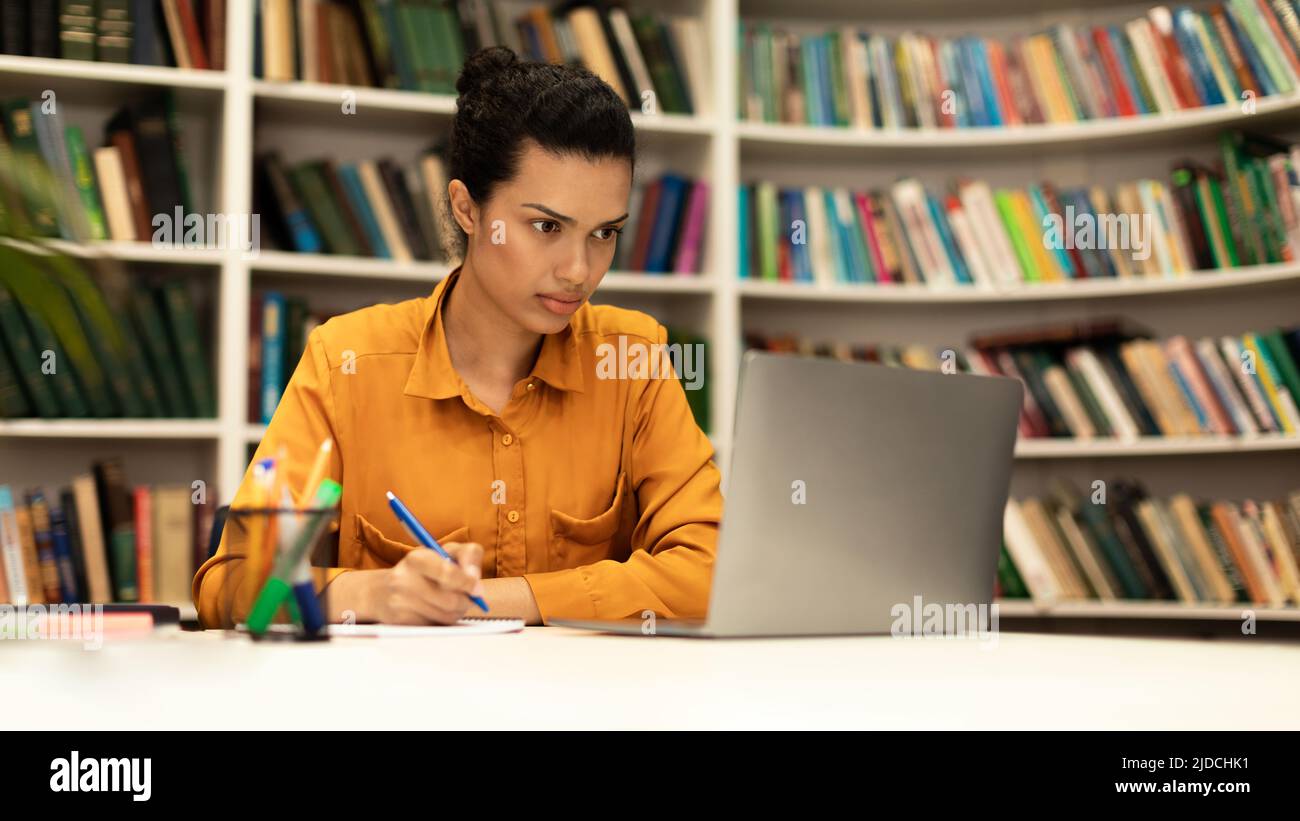 Focused woman using laptop and writing in notebook, studying online in ...