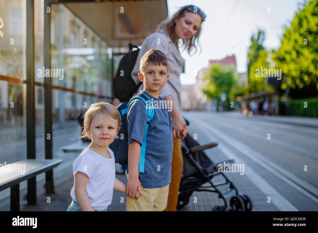 Young mother commuter with little kids on the way to school, waiting ...