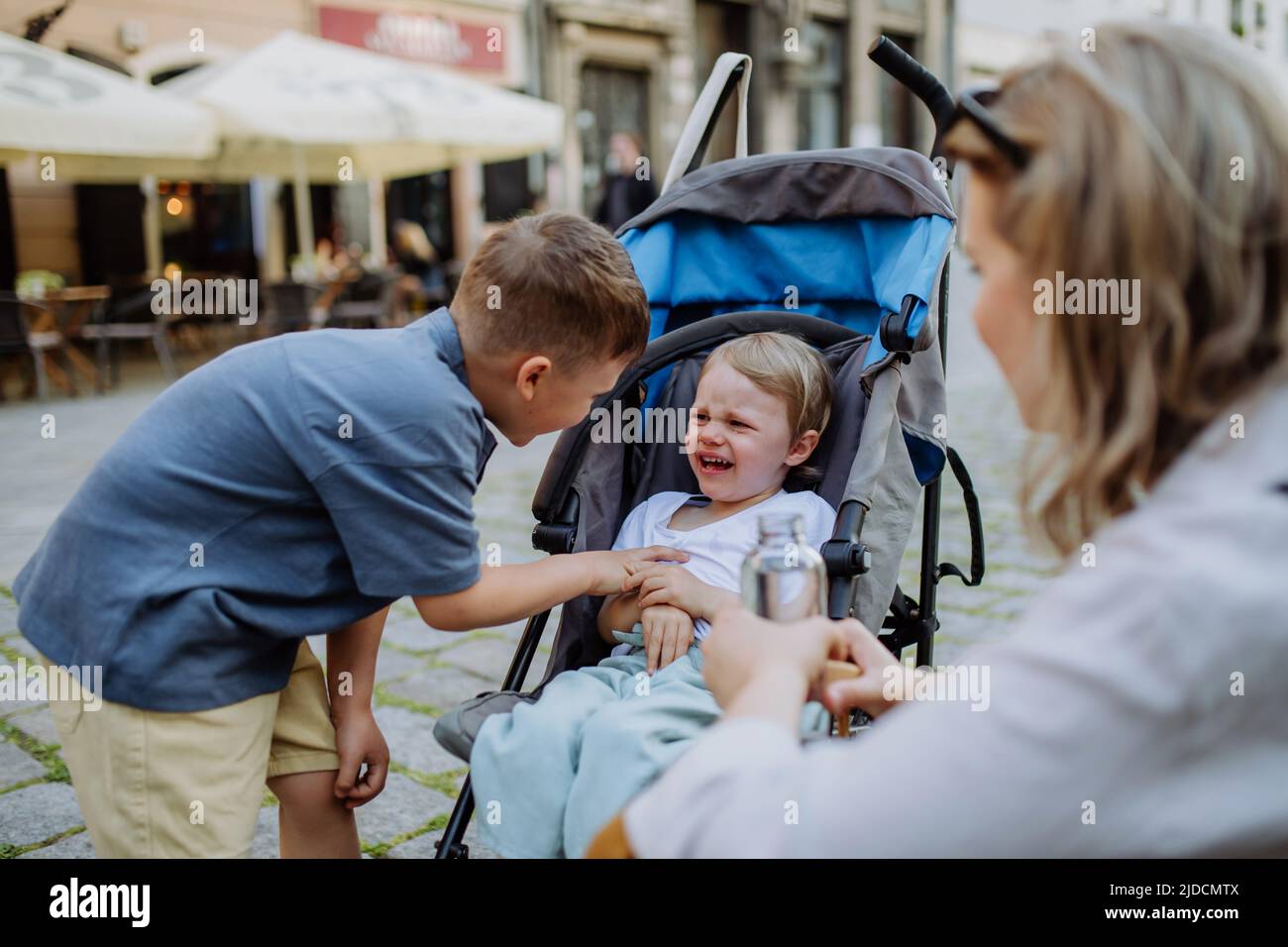 Mother and little brother calming a crying girl sitting in a stroller ...