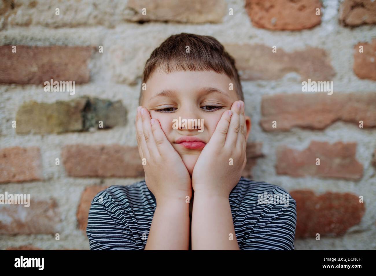 Little boy standing by brick wall and making funny faces in street ...