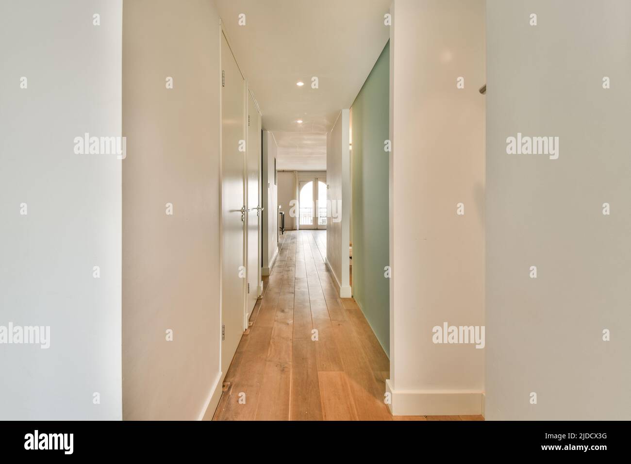 Narrow corridor with white walls and doors leading to spacious room ...