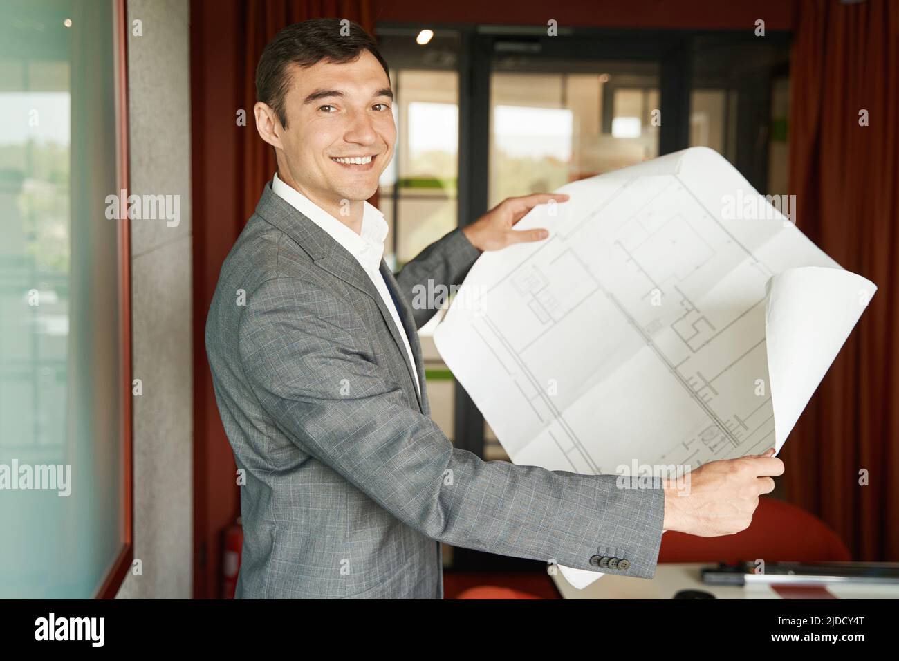 Pleased project manager holding building layout and smiling Stock Photo ...