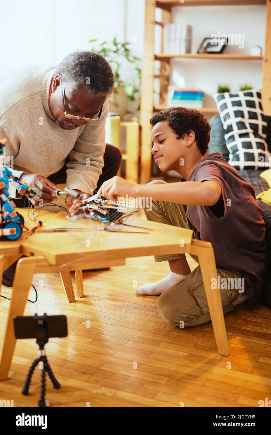 A grandfather showing his grandchild how to make a robot while sitting ...