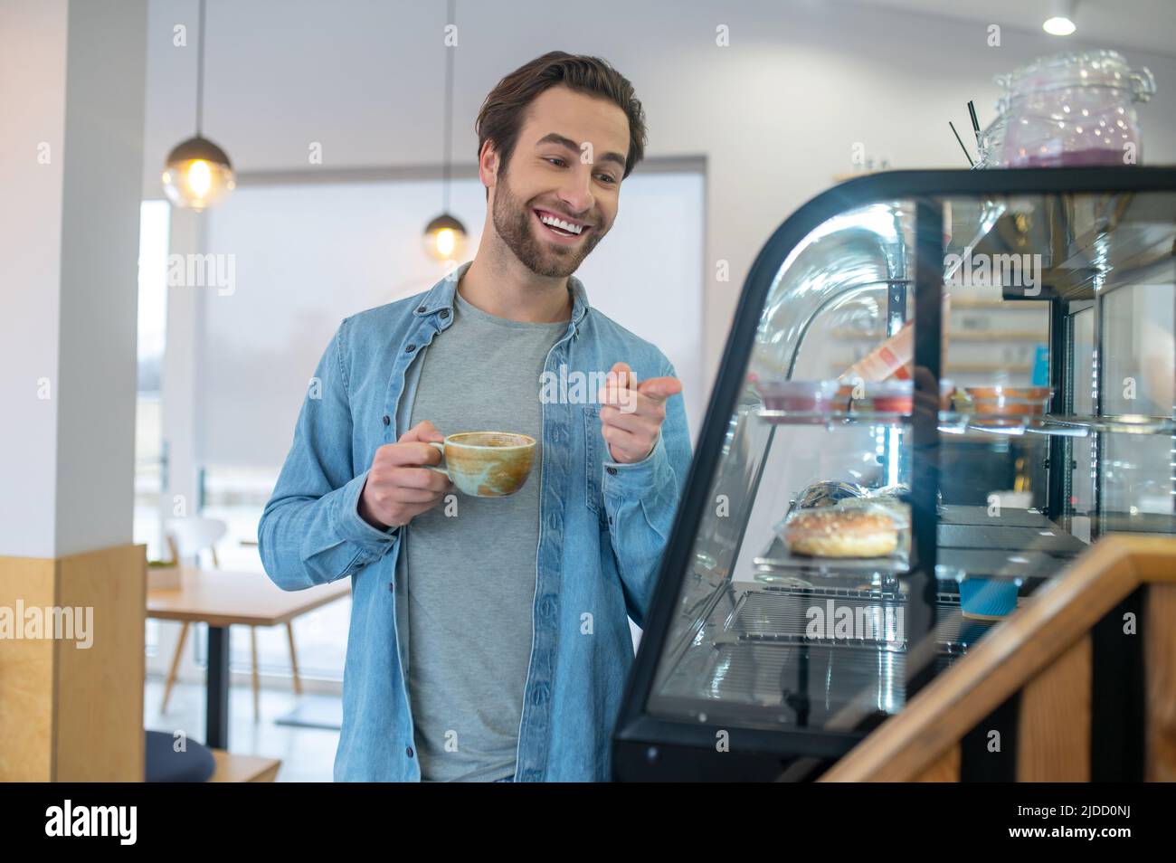 Man with coffee pointing at food display Stock Photo - Alamy