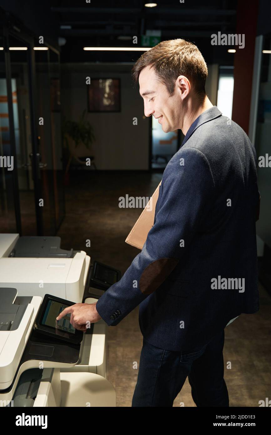 Smiling man choosing settings on office printer Stock Photo - Alamy
