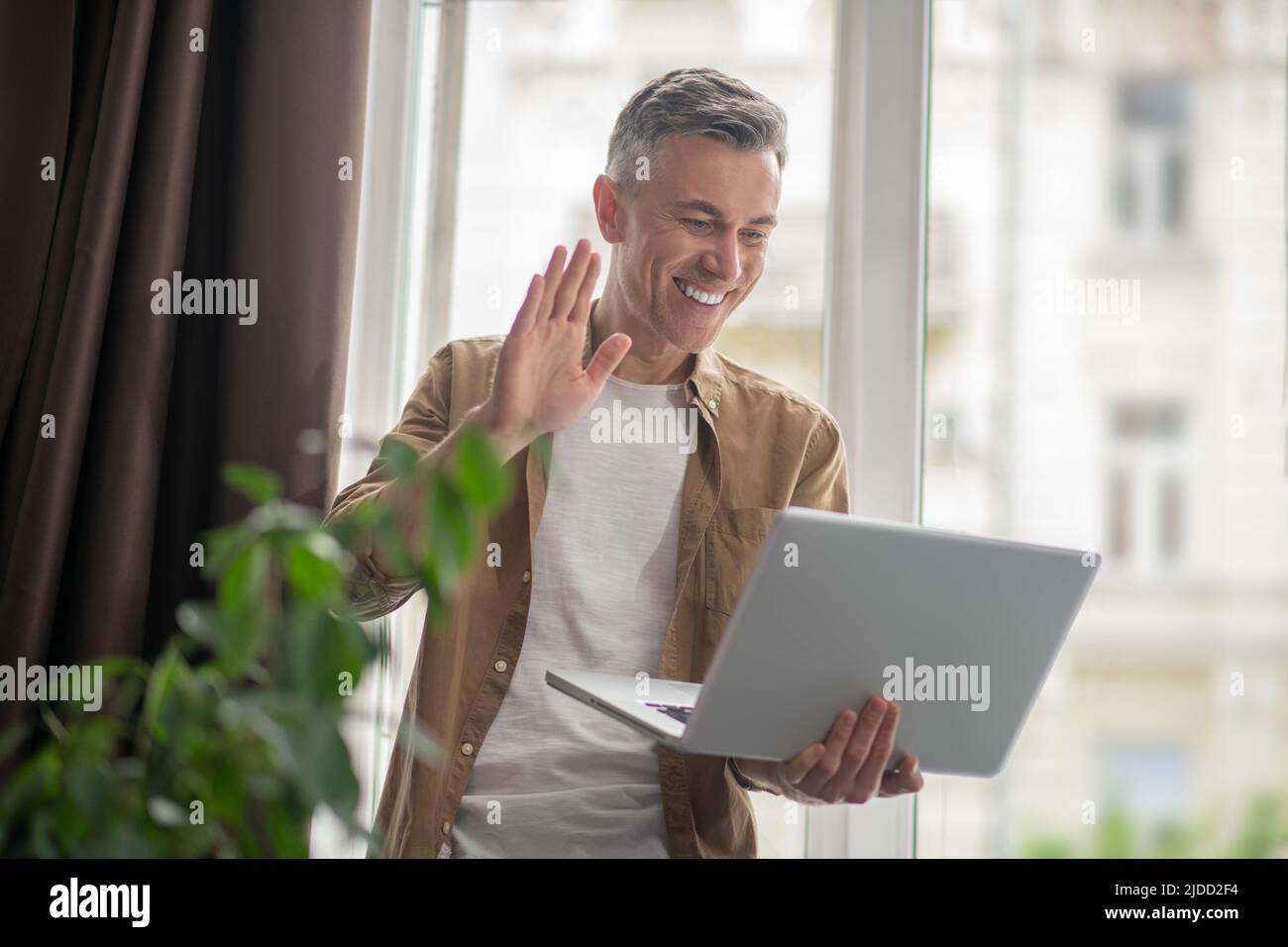 Man standing greeting waving smiling at laptop Stock Photo - Alamy