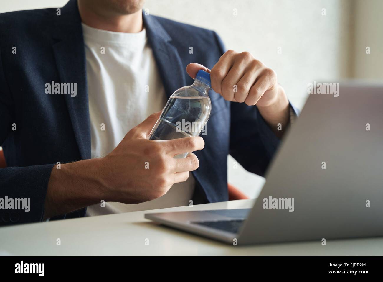 Worker opening bottle of water in front of laptop Stock Photo - Alamy