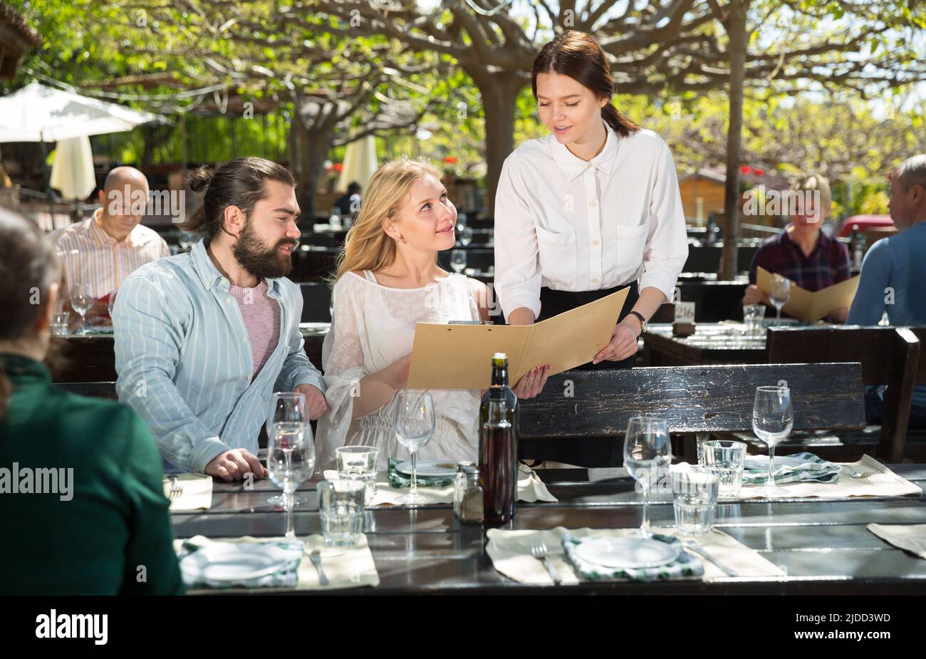 Charming young waiter and couple at open-air restaurant summer Stock ...