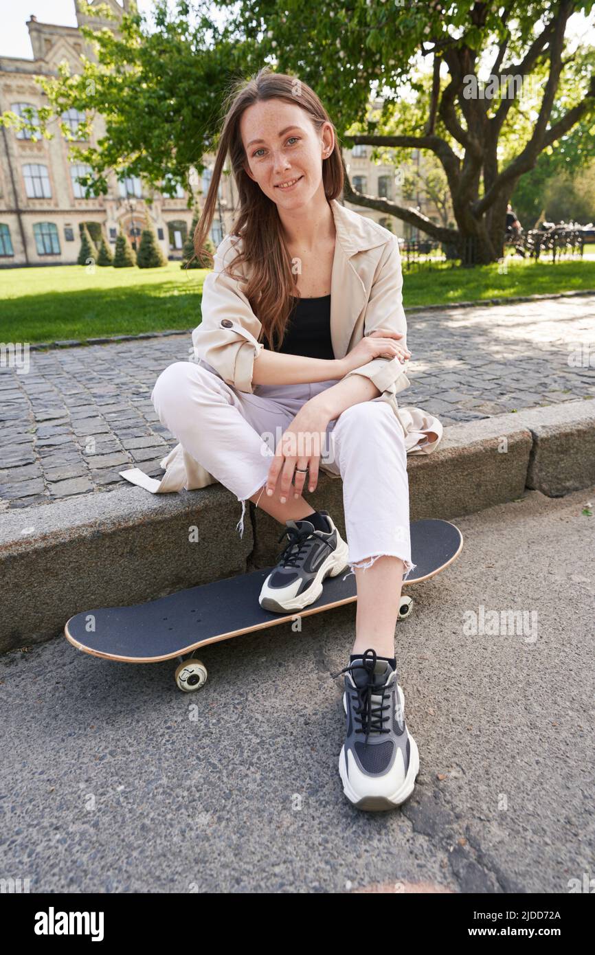 Lady sits on sidewalk in park putting feet on skateboard Stock Photo ...