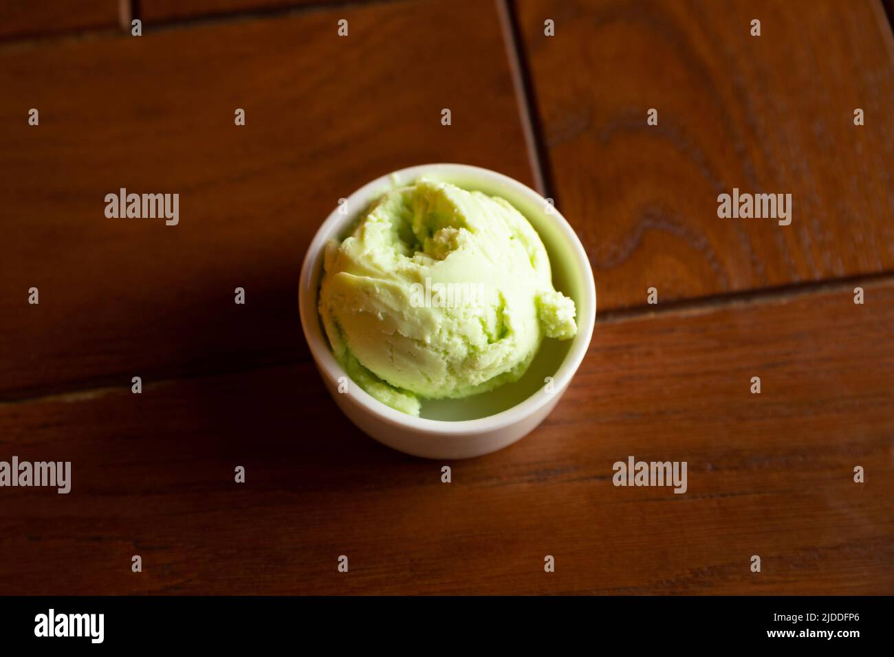 A scoop of pistachio ice cream in a bowl on a wooden table. Top view ...